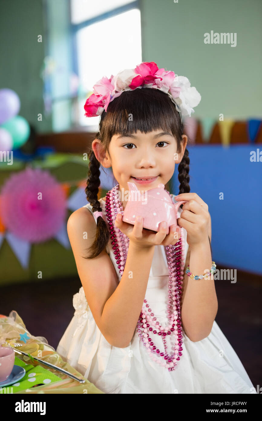 Portrait of cute girl holding toy teapot during birthday party at home ...