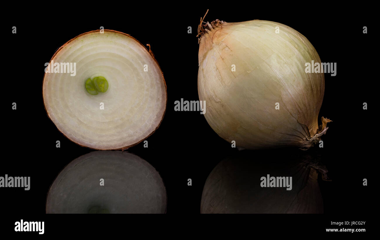 Whole and cut onion on black background reflecting on a glass surface ...