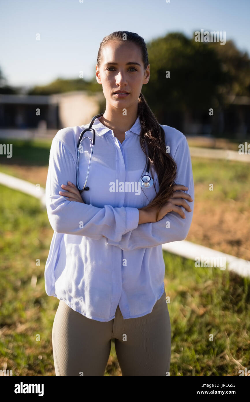 Portrait of female vet with arms crossed standing on field at barn ...