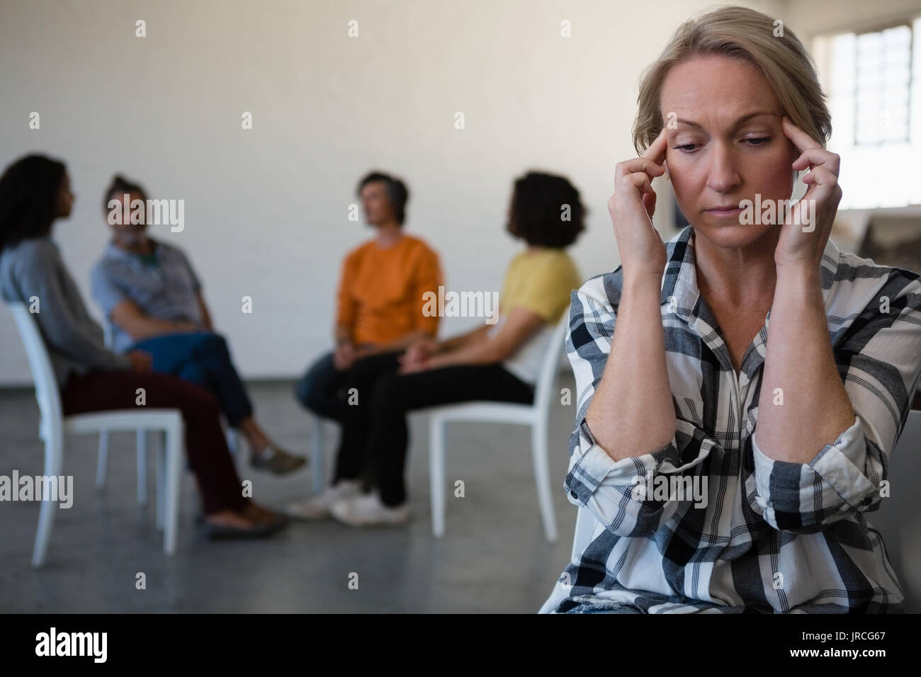 Tensed woman with head in hand while friends discussing in background ...