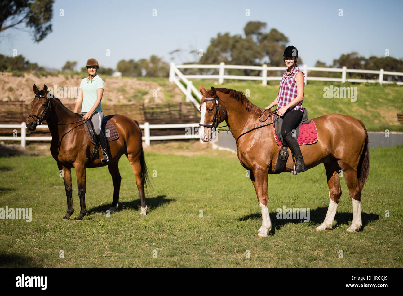 Female friends horseback riding during sunny day at paddock Stock Photo ...