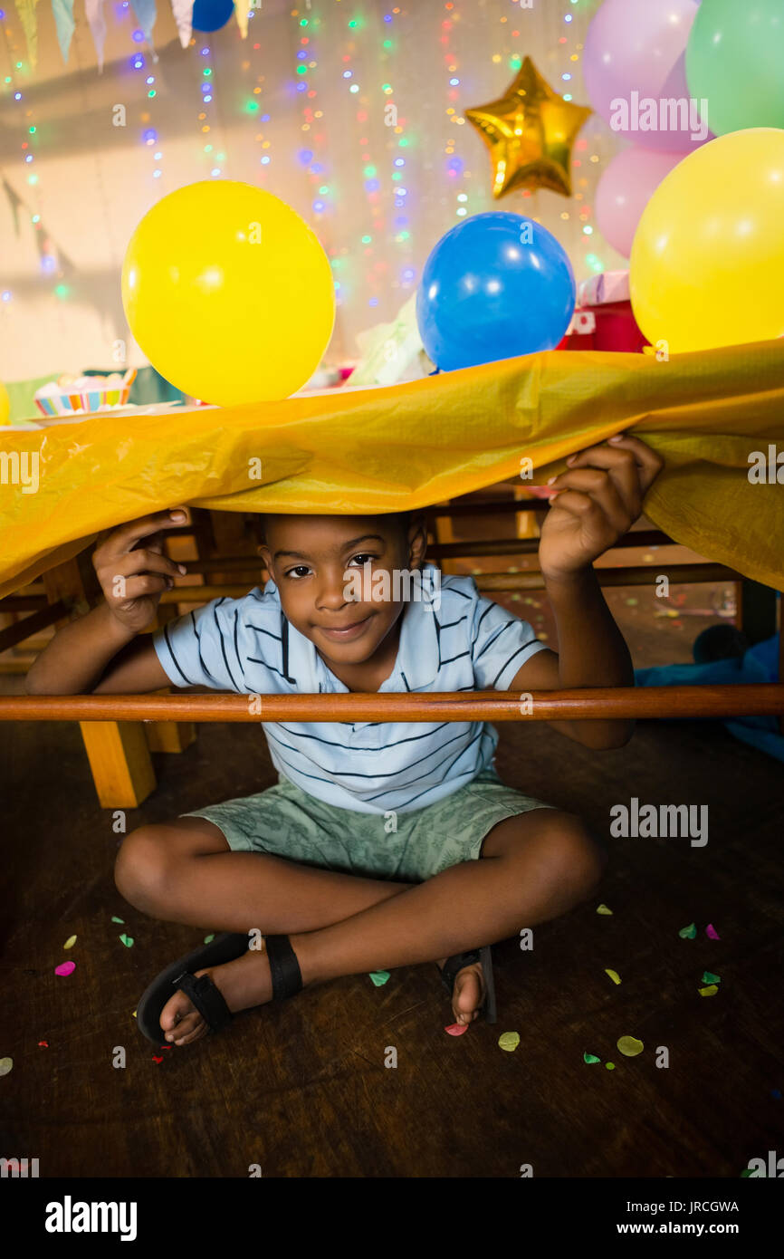 Portrait of cute boy sitting under table at home Stock Photo - Alamy