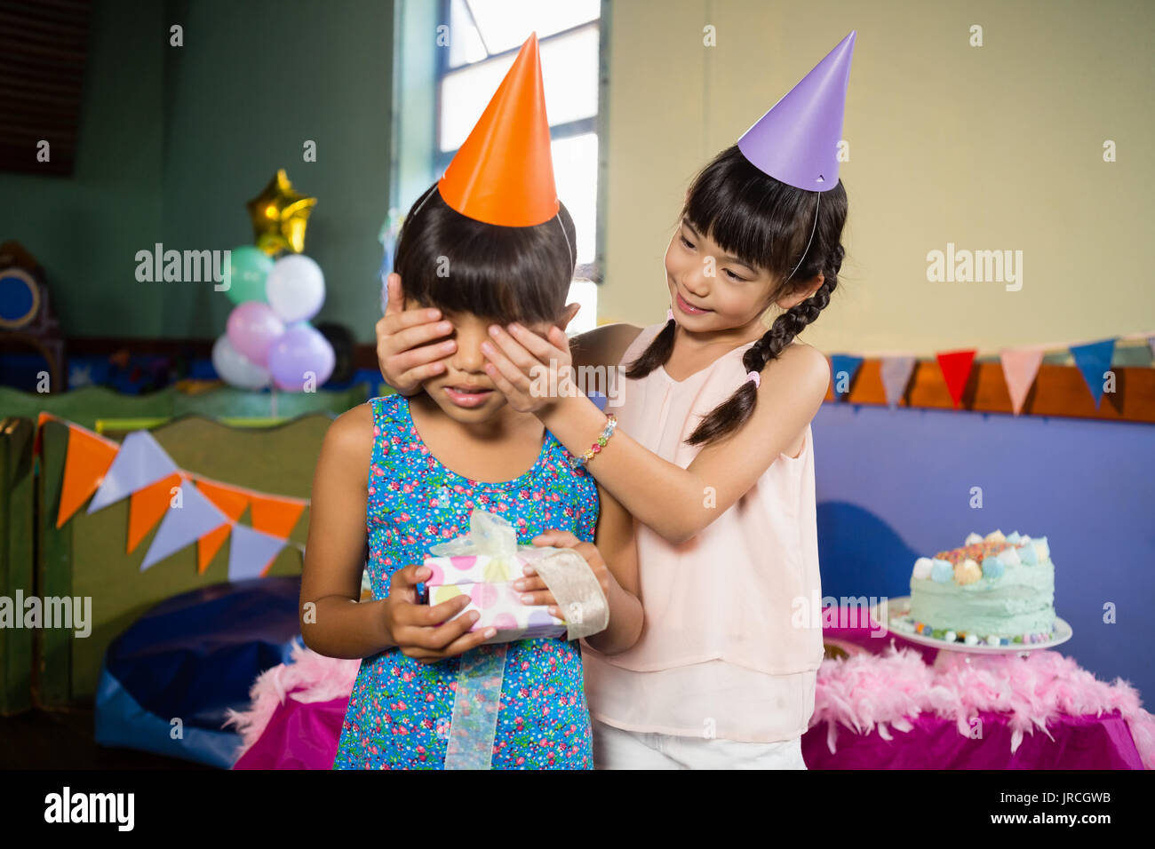 Smiling girl covering birthday girls eyes and offering a gift Stock ...