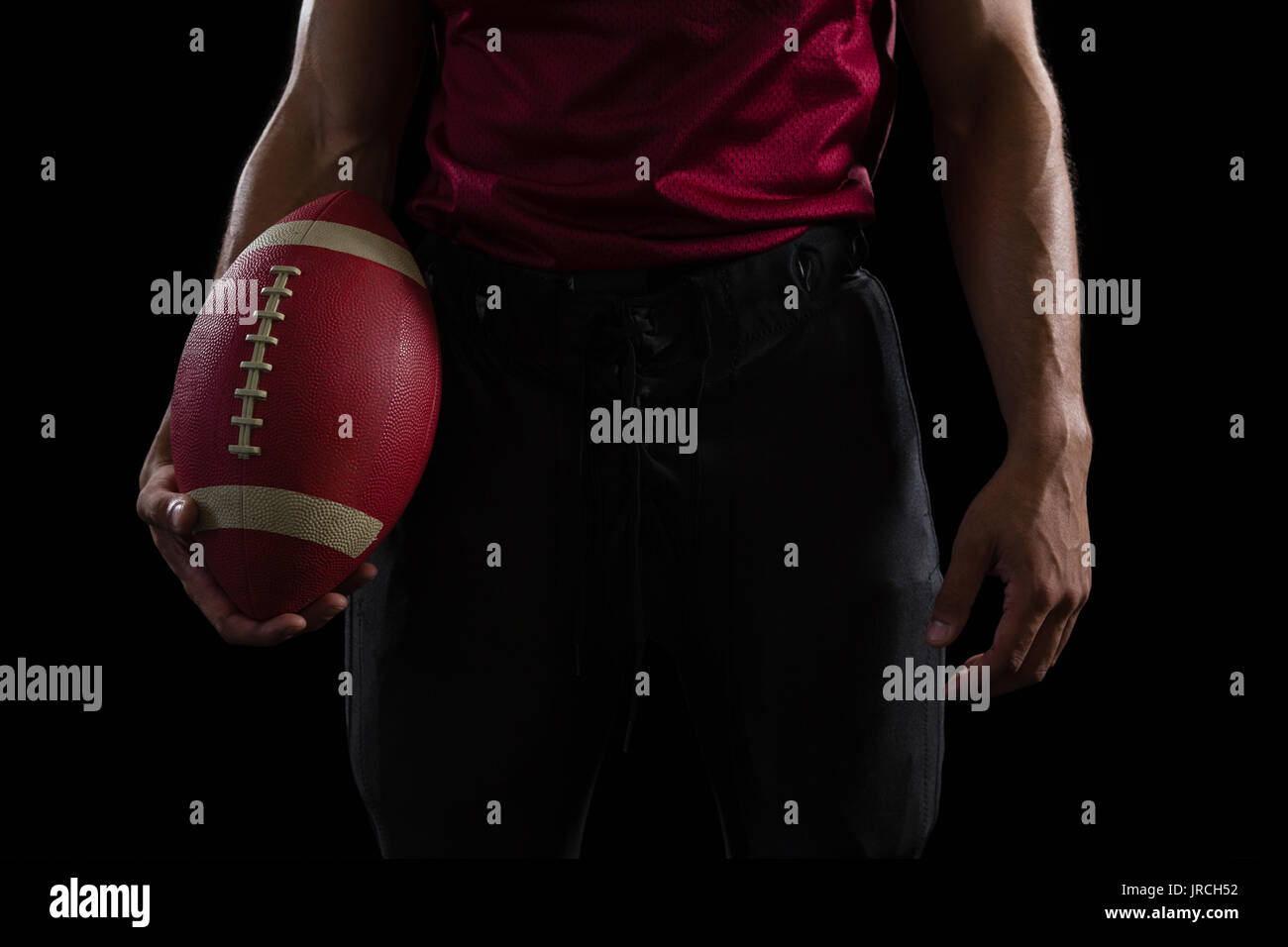 Mid section of American football player holding a ball in one hand ...