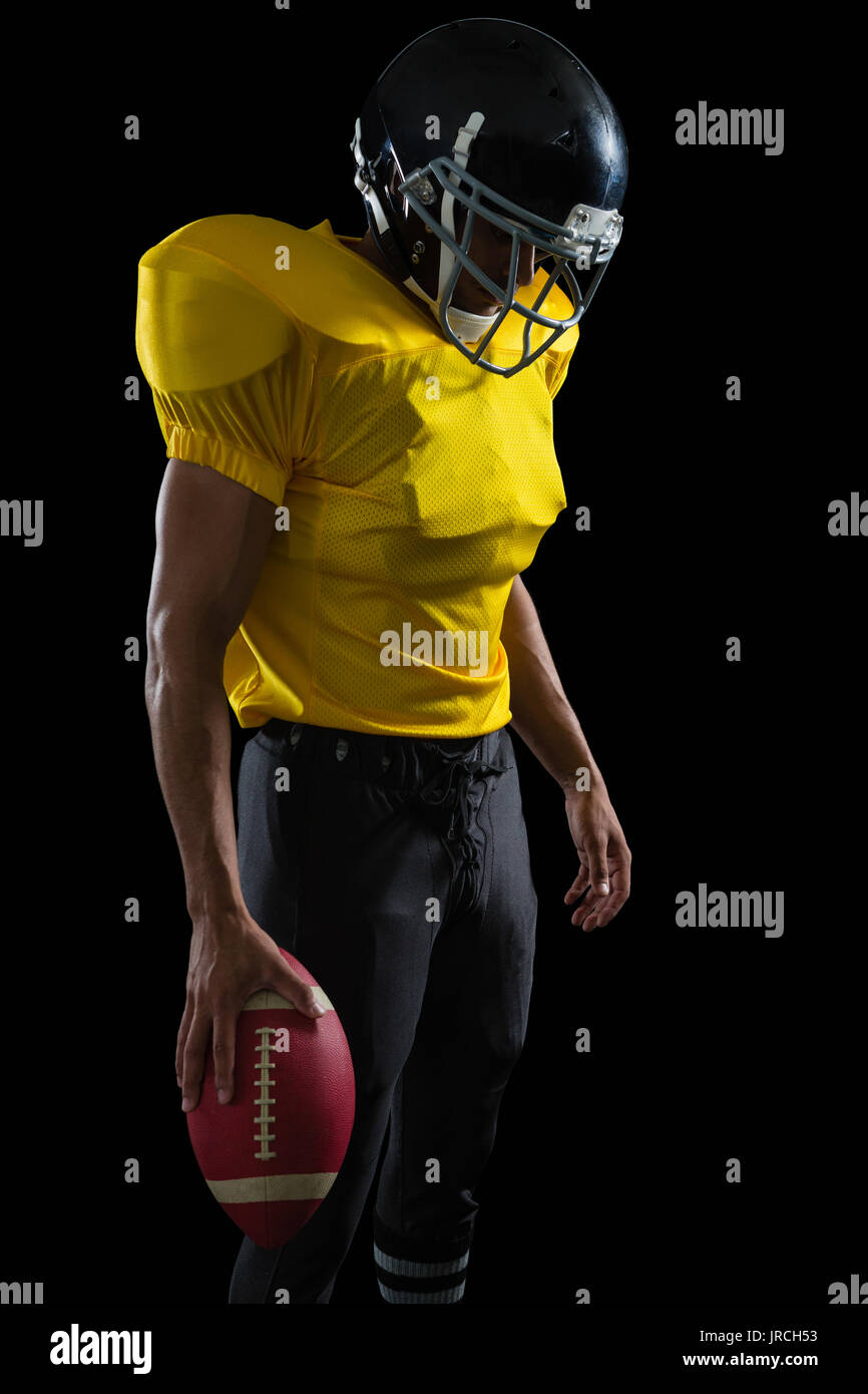 American football player holding a football in his hand against black ...