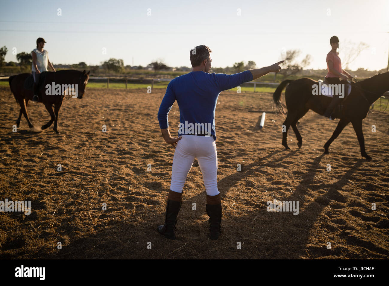 Male trainer guiding young women in riding horse at barn Stock Photo ...