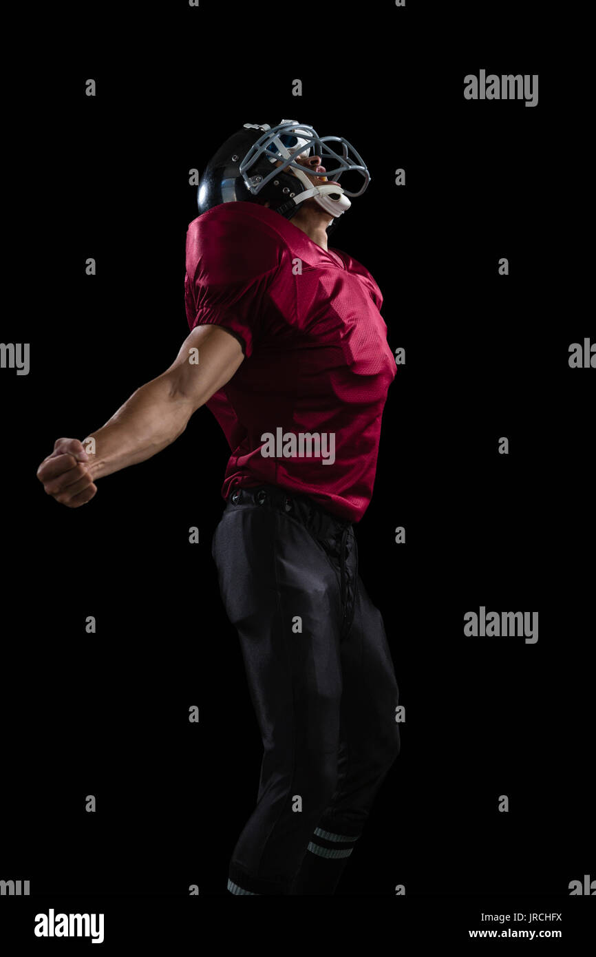American football player posing with arms stretched open against black ...