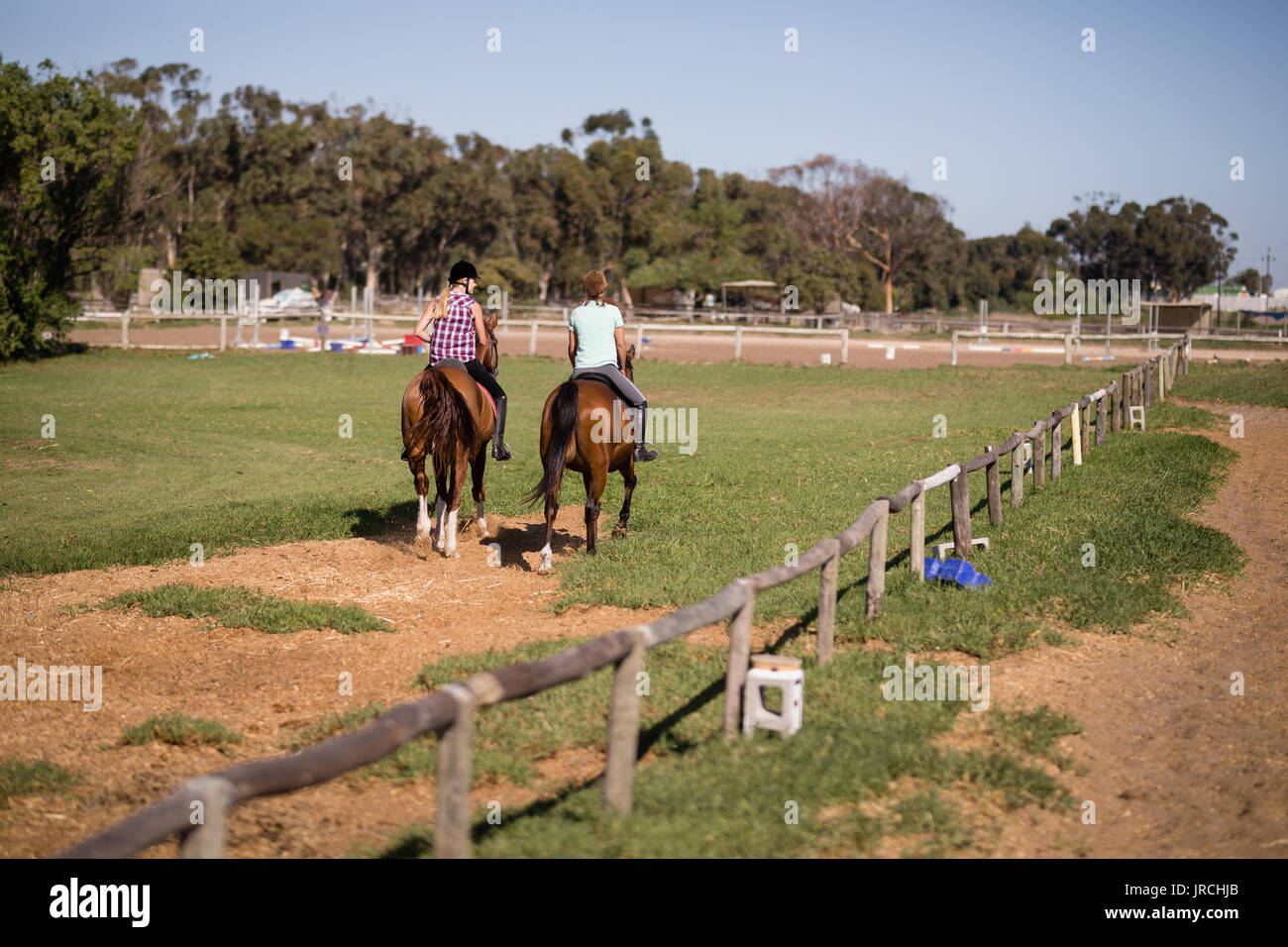 Female friends horseback riding at paddock during sunny day Stock Photo ...