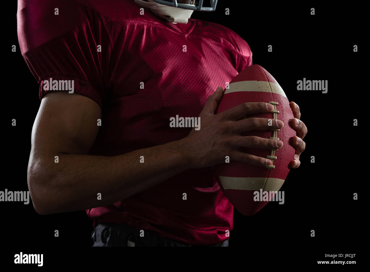 Mid section of American football player holding a ball in one hand ...