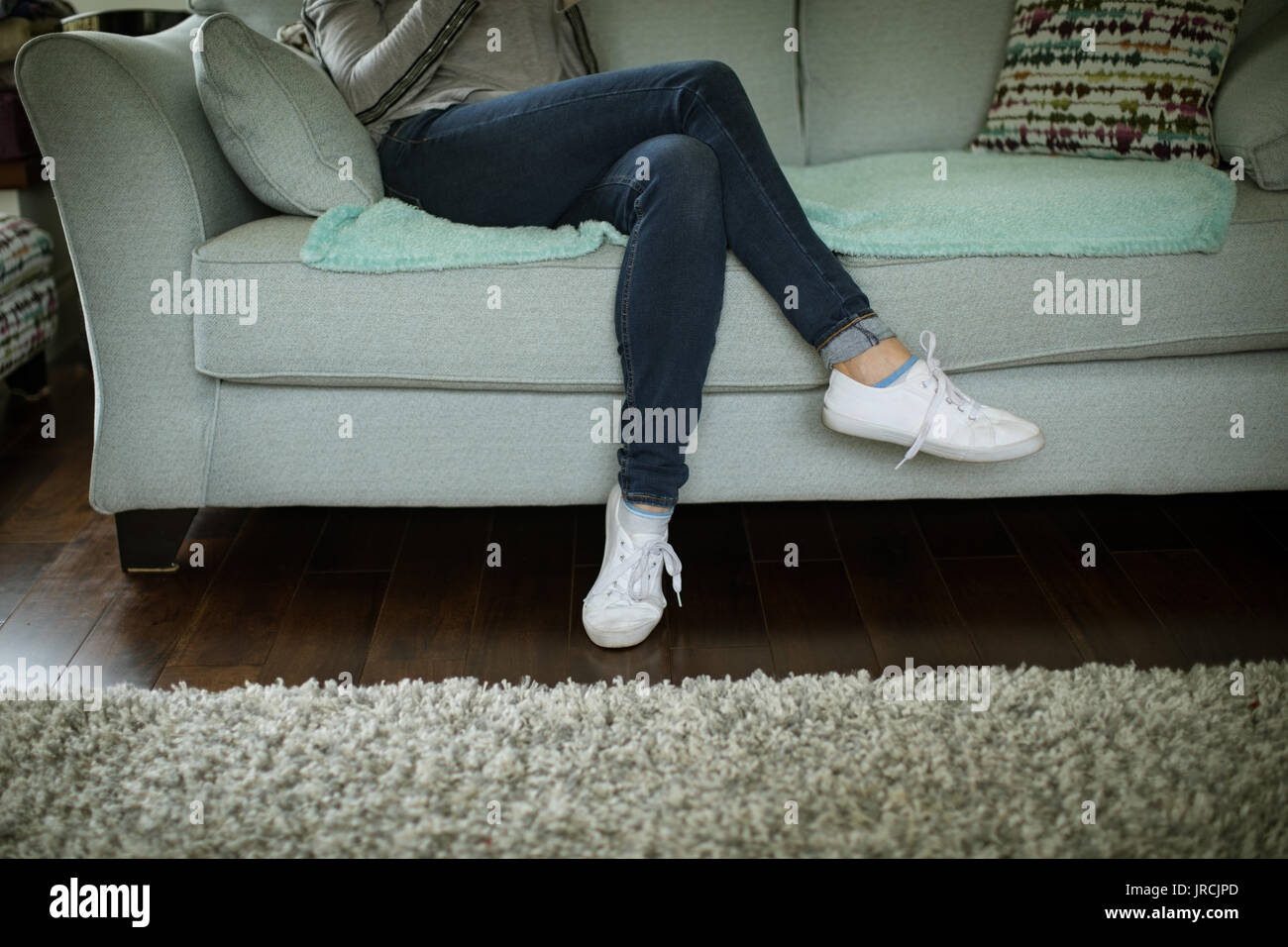 Low section of woman sitting on sofa at home Stock Photo - Alamy