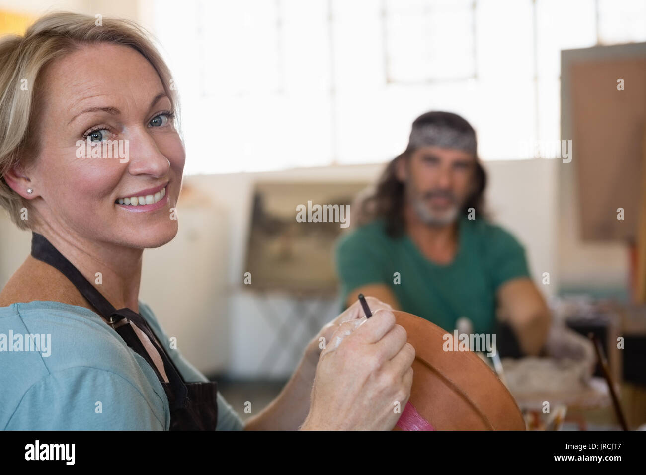 Portrait of woman decorating clay pot with student sitting in ...