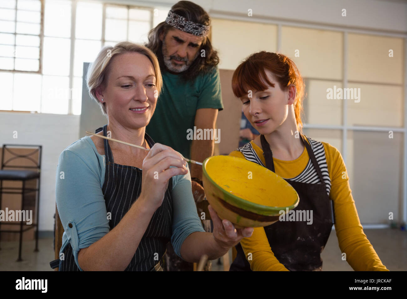 Adult students looking at teacher painting clay product in art class ...