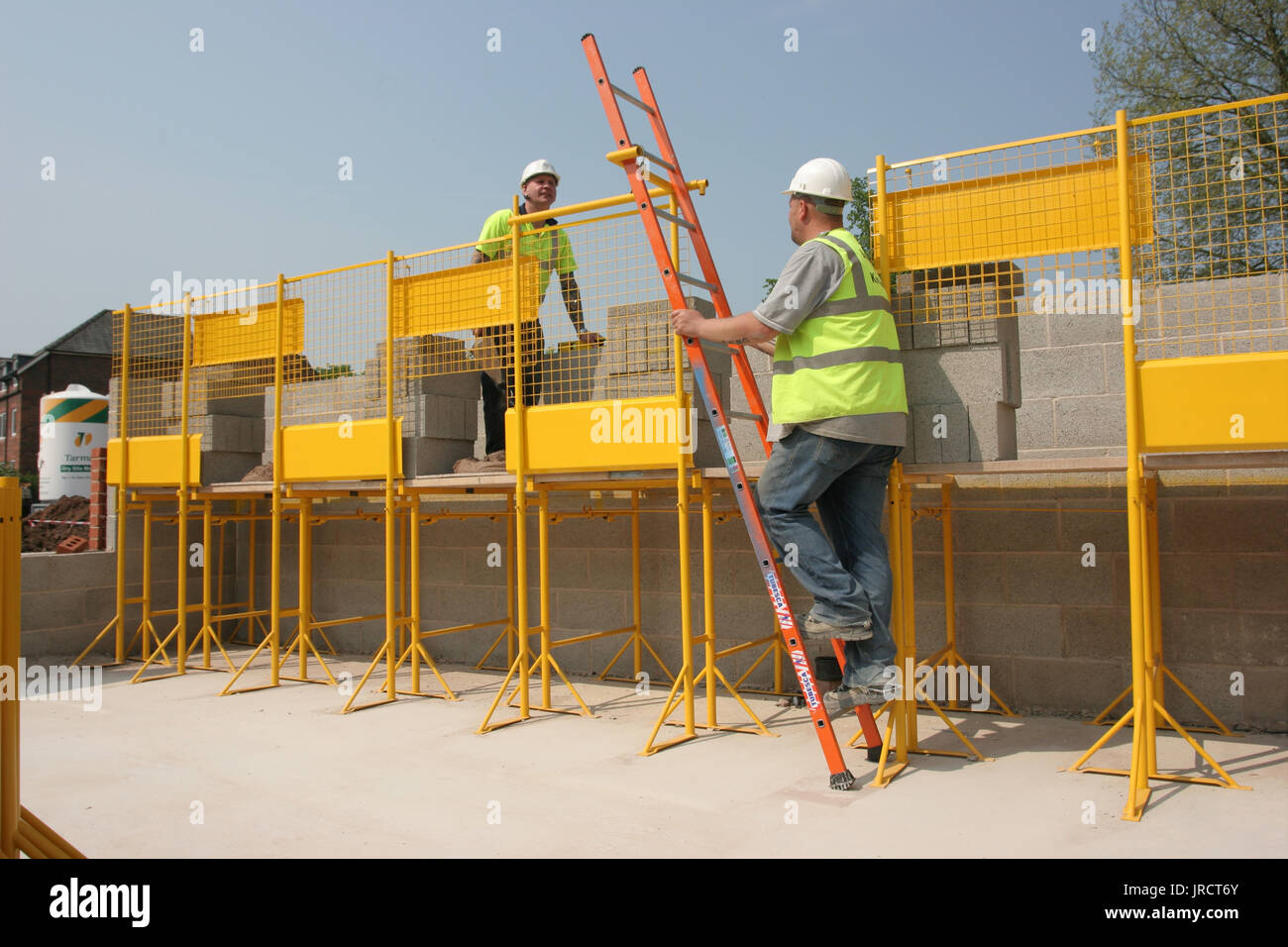 A bricklayer climbs a ladder to a fully protected work platform ...