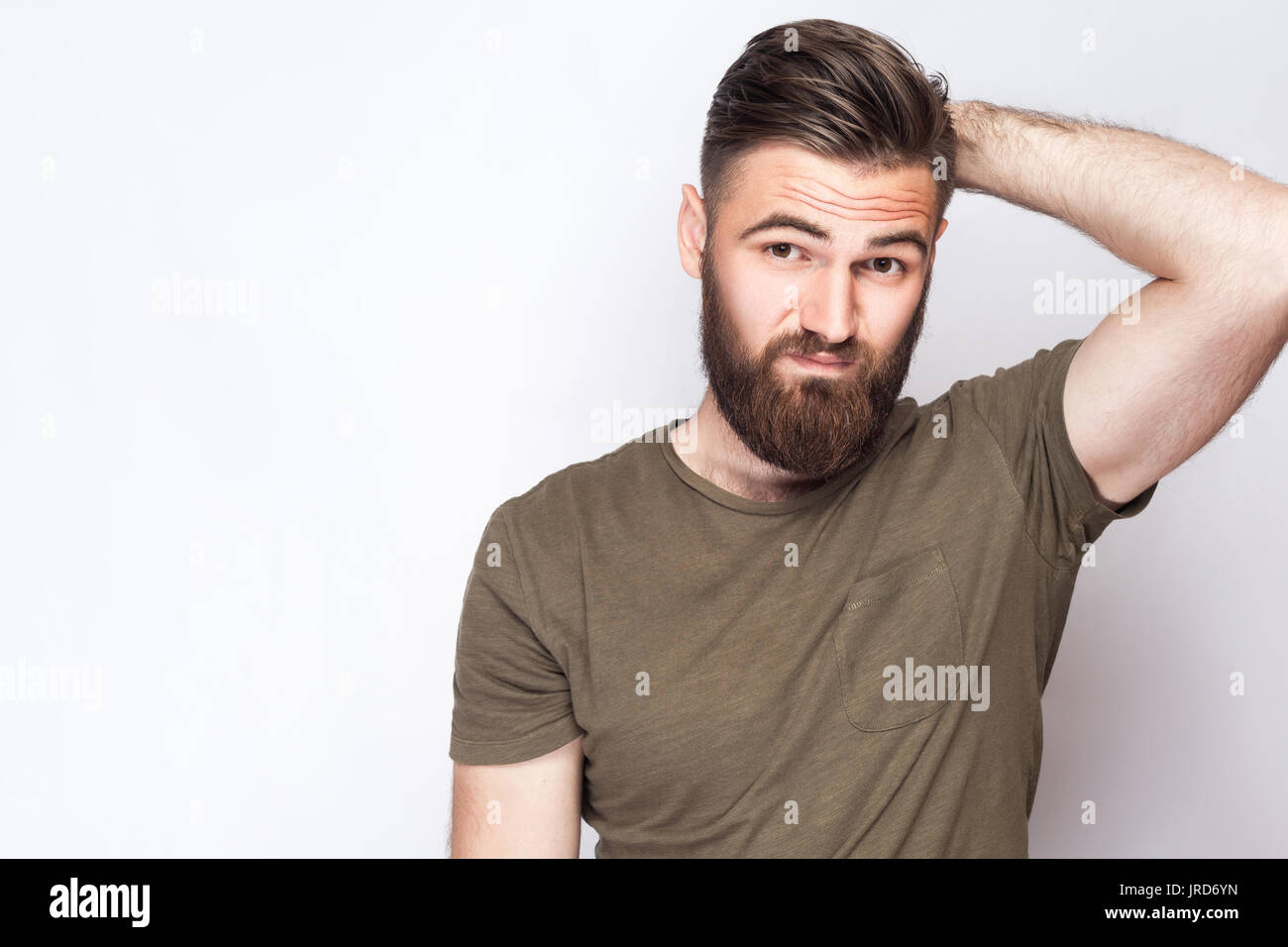 Portrait of thinking bearded man with dark green t shirt against light ...