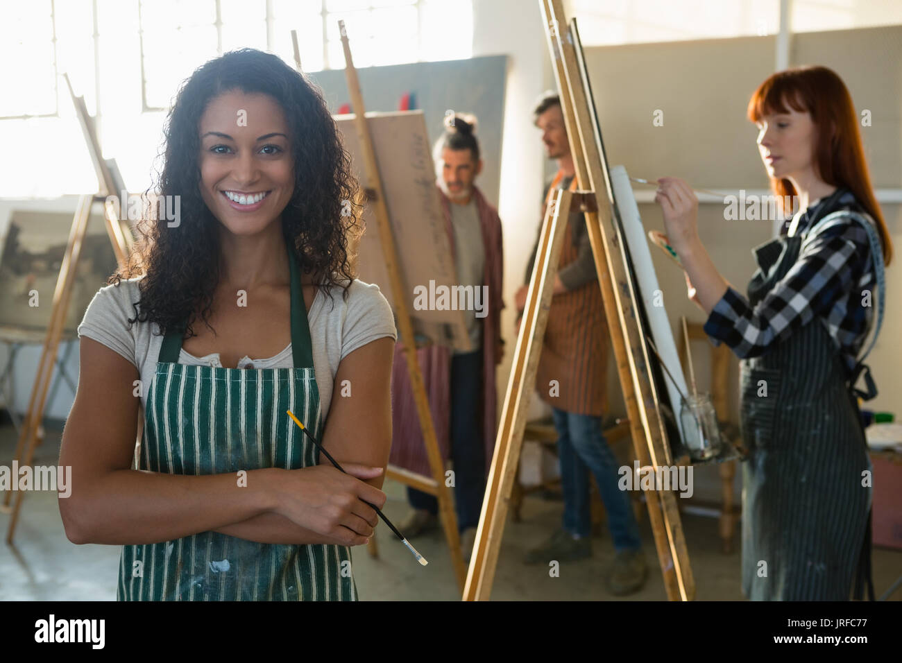 Portrait of smiling female artist with friends painting in background ...