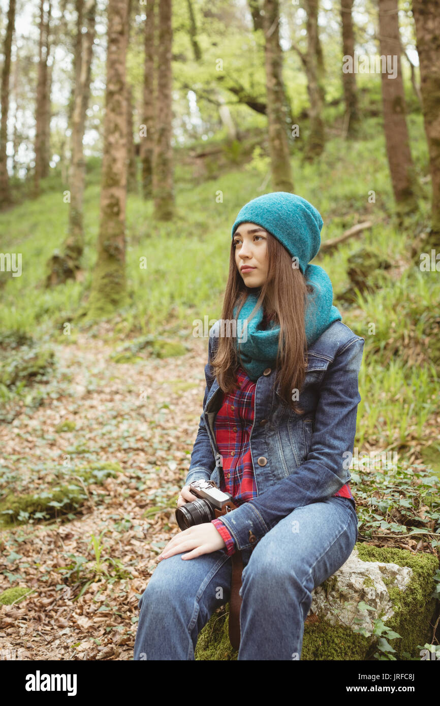 Thoughtful woman sitting on rock at forest Stock Photo - Alamy