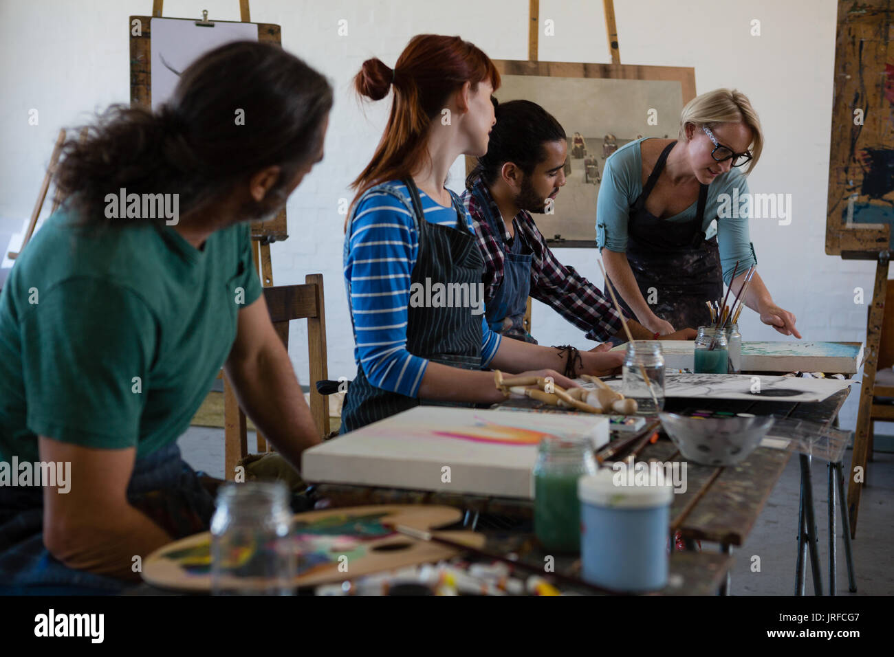 Teacher examining painting while standing by student in art class Stock ...