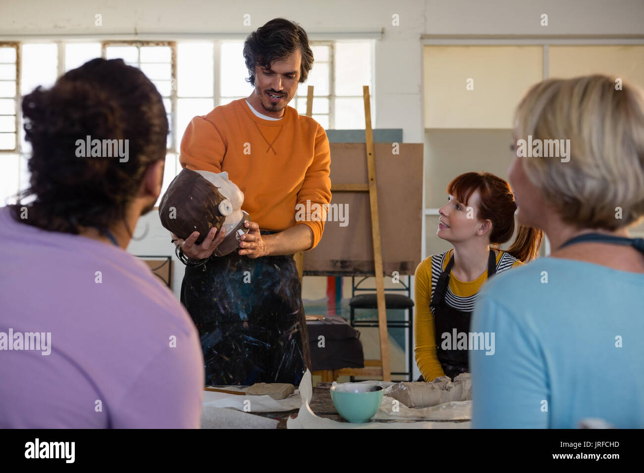 Male teaching holding sculpture while explaining students in art class ...