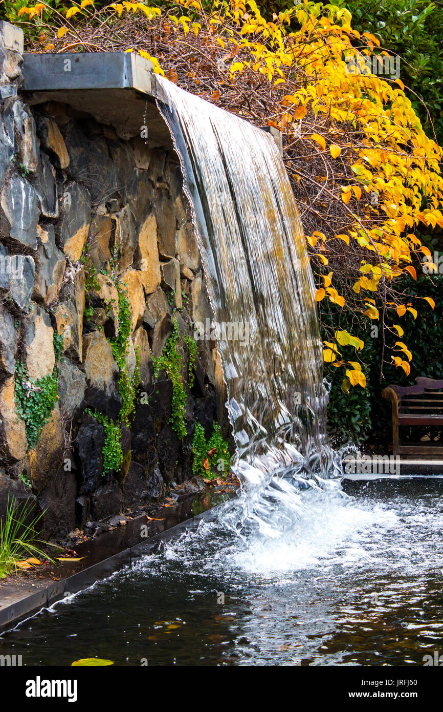 Garden waterfall over sandstone rocks into small pond with autumn fall ...