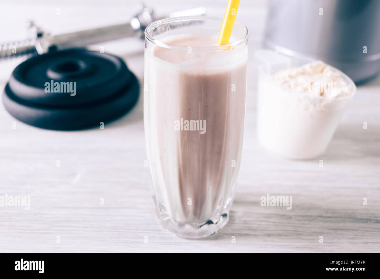 Protein cocktail in a glass with a straw, scoop and dumbbell on a white ...