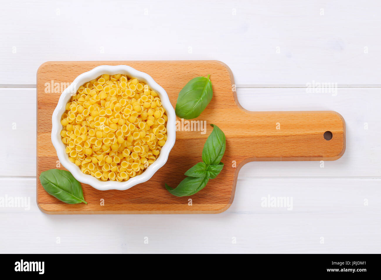 bowl of small pasta shells on wooden cutting board Stock Photo - Alamy