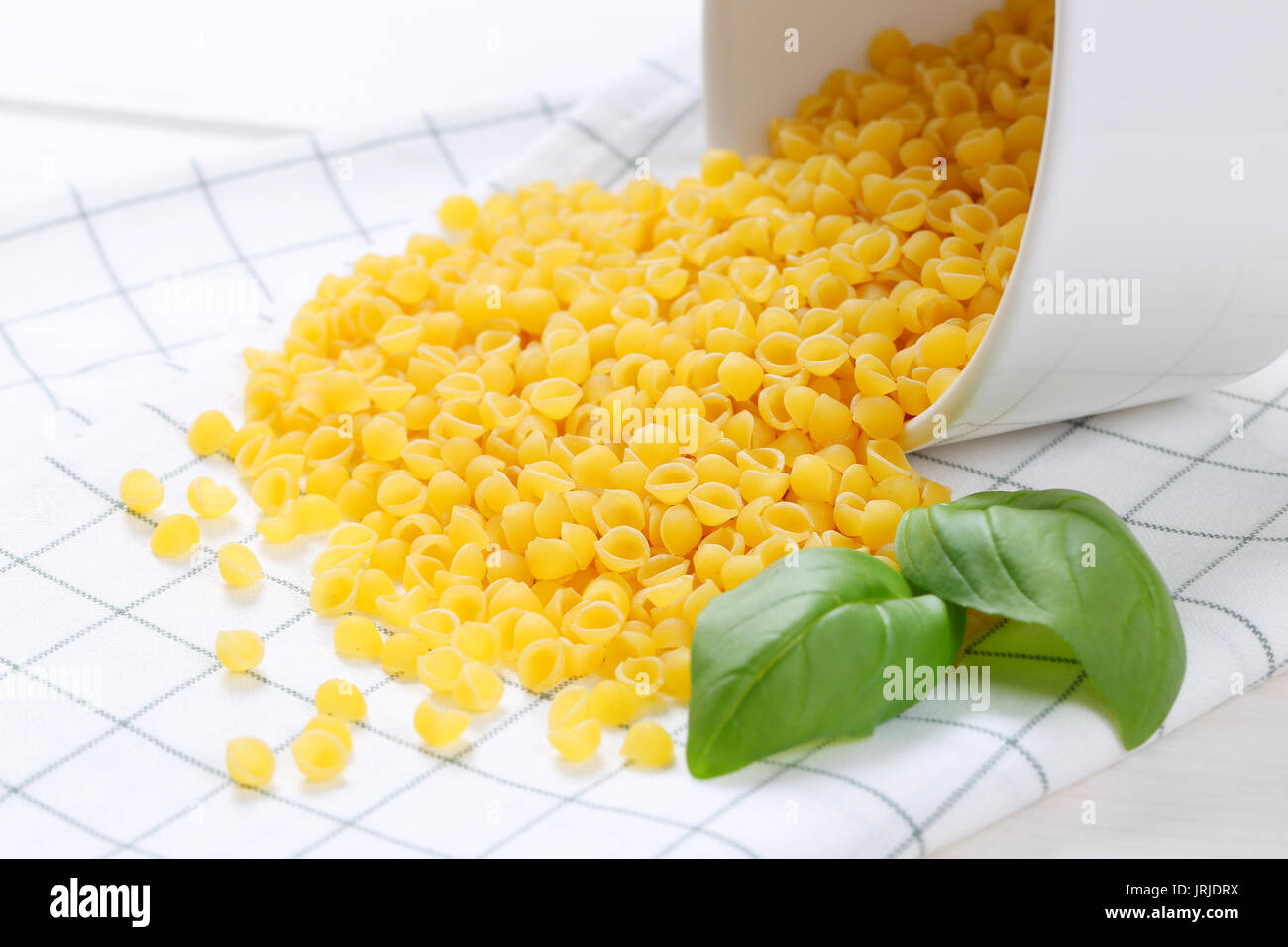 bowl of small pasta shells spilt out on checkered dishtowel - close up ...