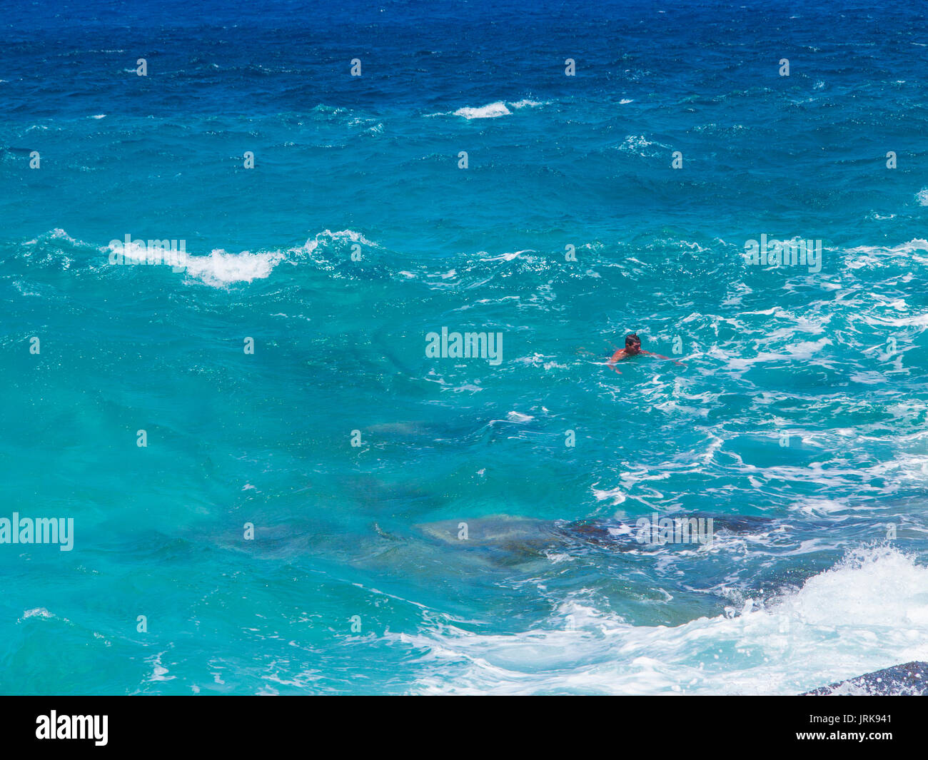 A lone person swimming in a very rough sea with big waves after a storm ...