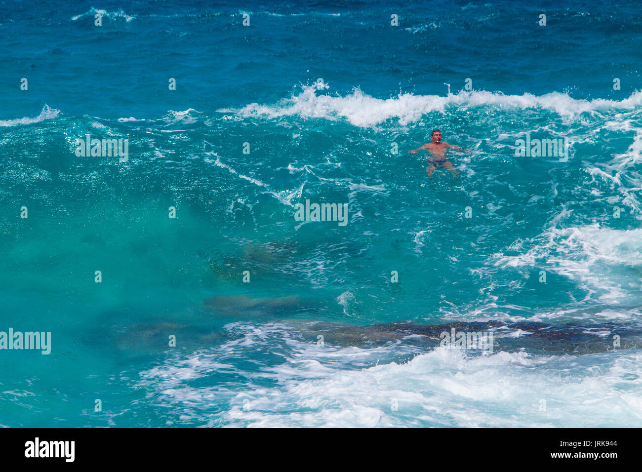A lone person swimming in a very rough sea with big waves after a storm ...
