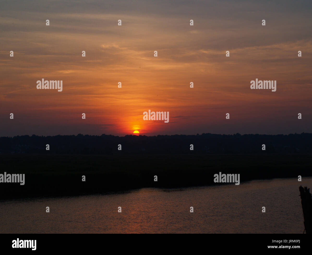 The setting sun casts an orange glow on the horizon overlooking a tidal ...