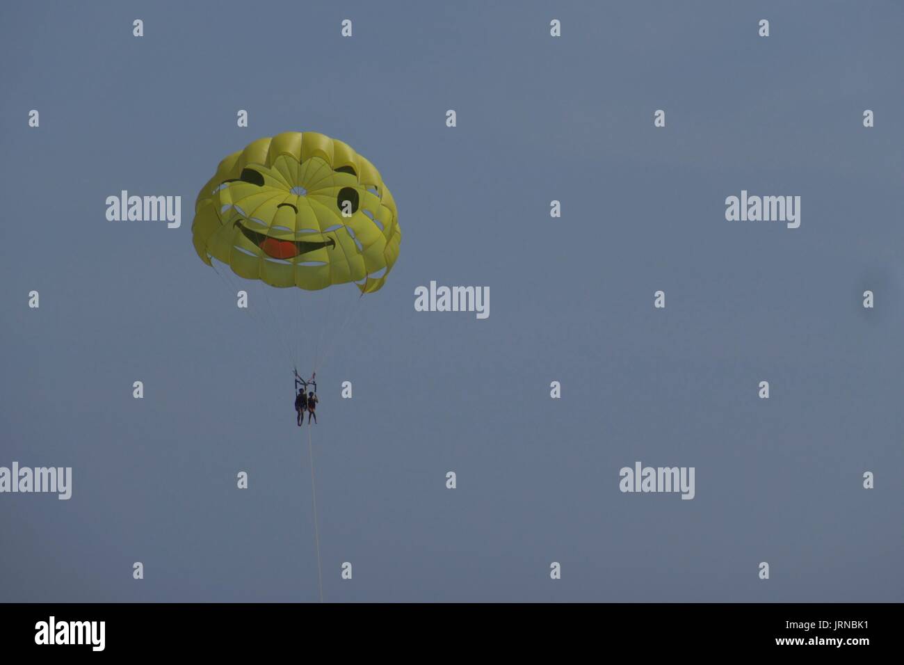 Distant view of parasailing with yellow smiley face parasail against ...