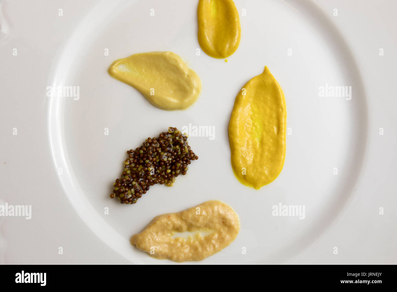 Smears of various mustards on white china plate over rustic wooden ...