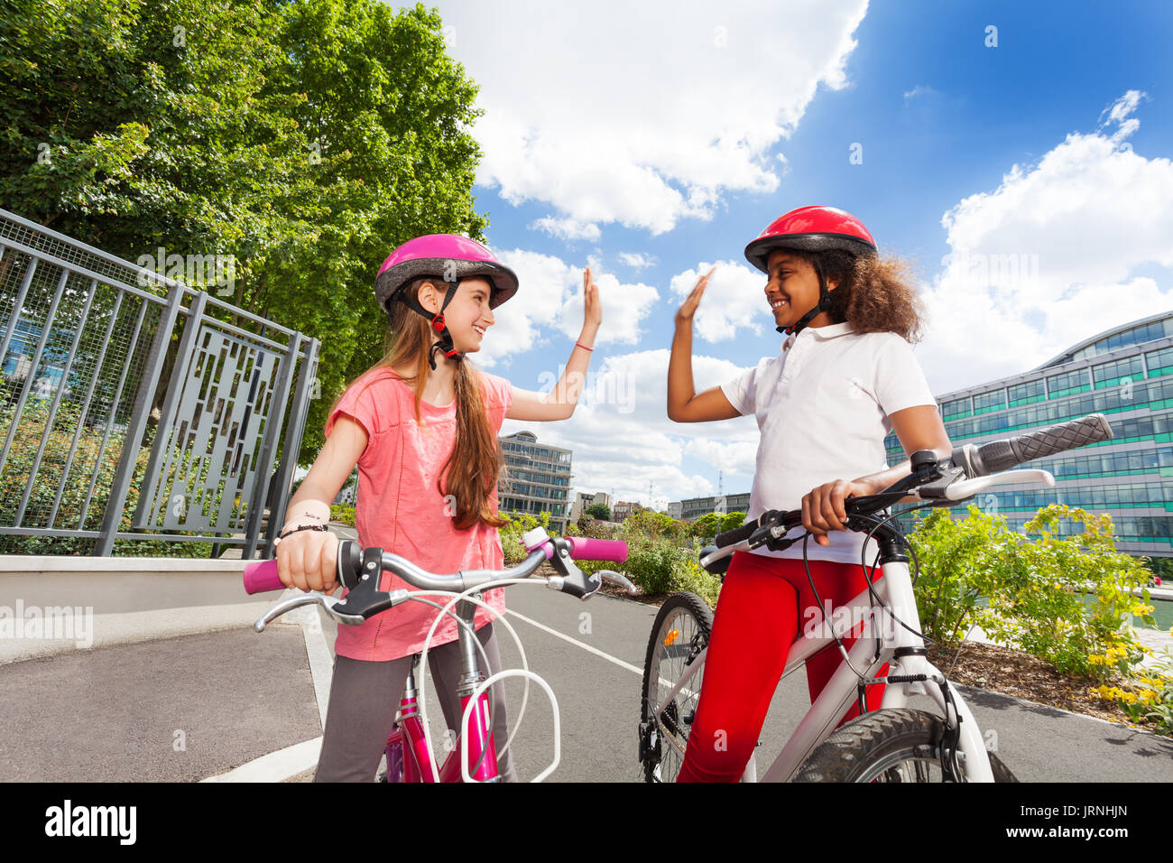 Portrait of two preteen girl friends, bicycle riders in helmets, giving ...