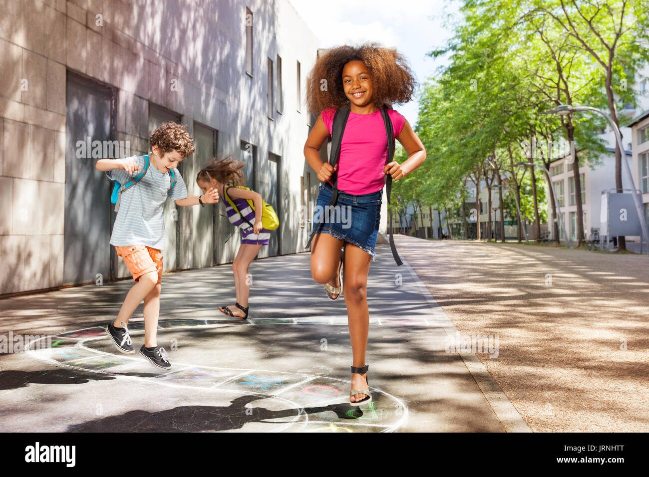 Portrait of kids jumping on the hopscotch squares and letters looking ...