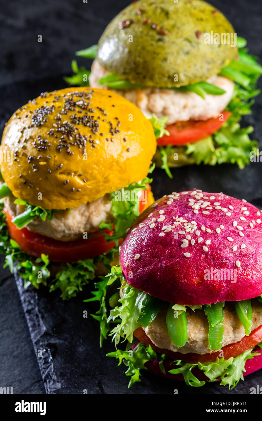 Colored green, yellow and purple burgers on slate board. Close up Stock ...