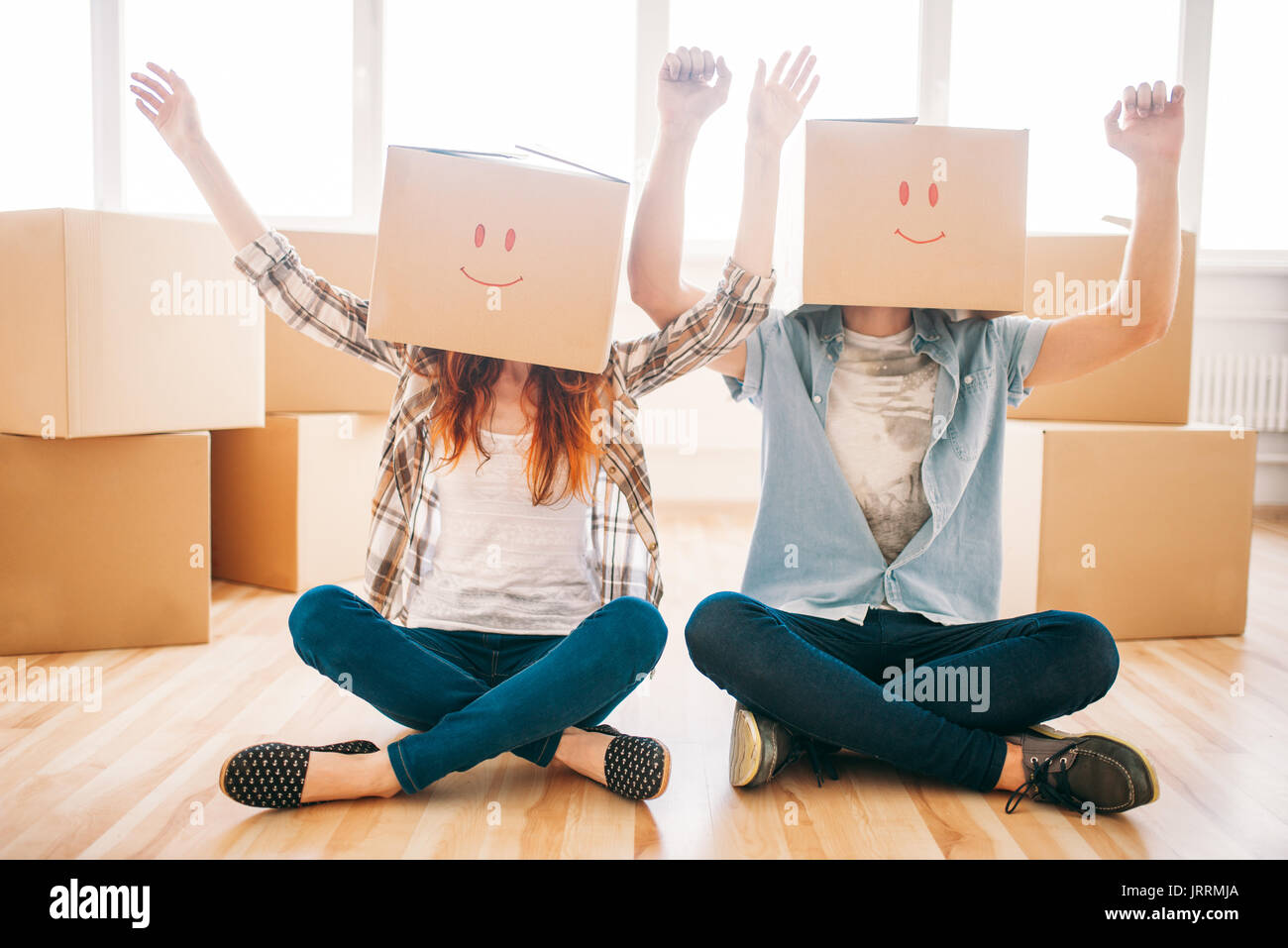 Playful couple with cardboard boxes on their heads sitting on the floor ...