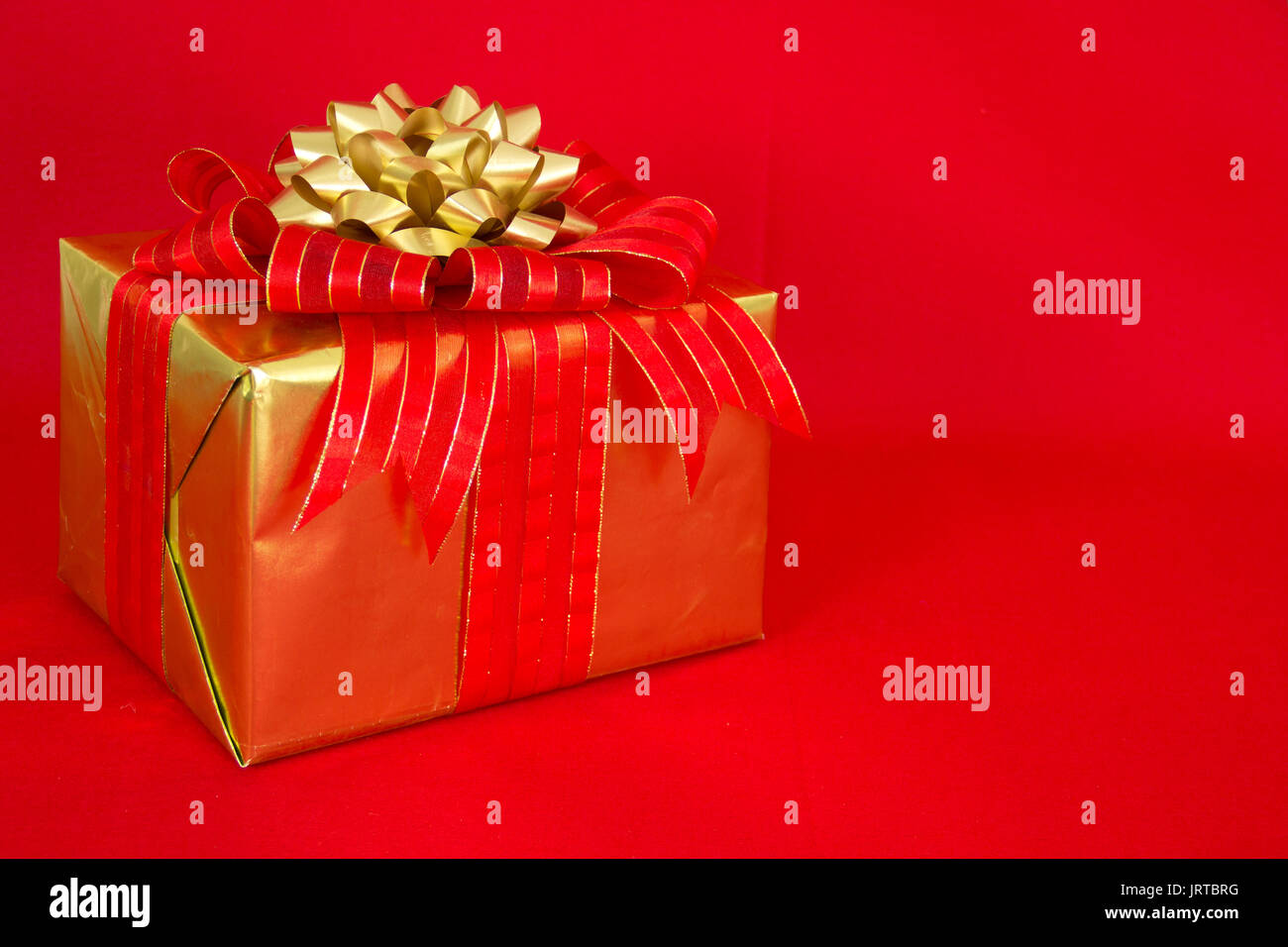 A gold foil-wrapped gift is topped by a red striped bow and ribbons and ...