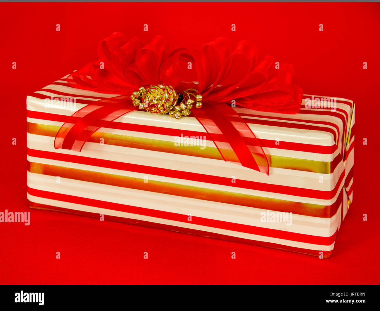 A gift wrapped in red, gold and white striped paper is topped by a red ...