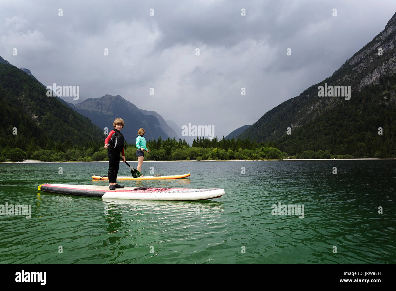 Mother and son in a wet suit paddling on SUP on alpine lake, Lago di ...