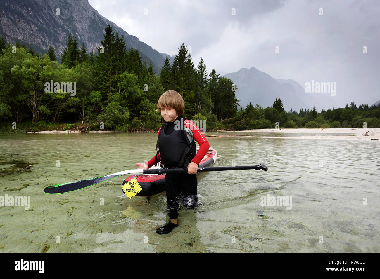 Young boy carrying a paddle and pulling a SUP in the clear water of ...