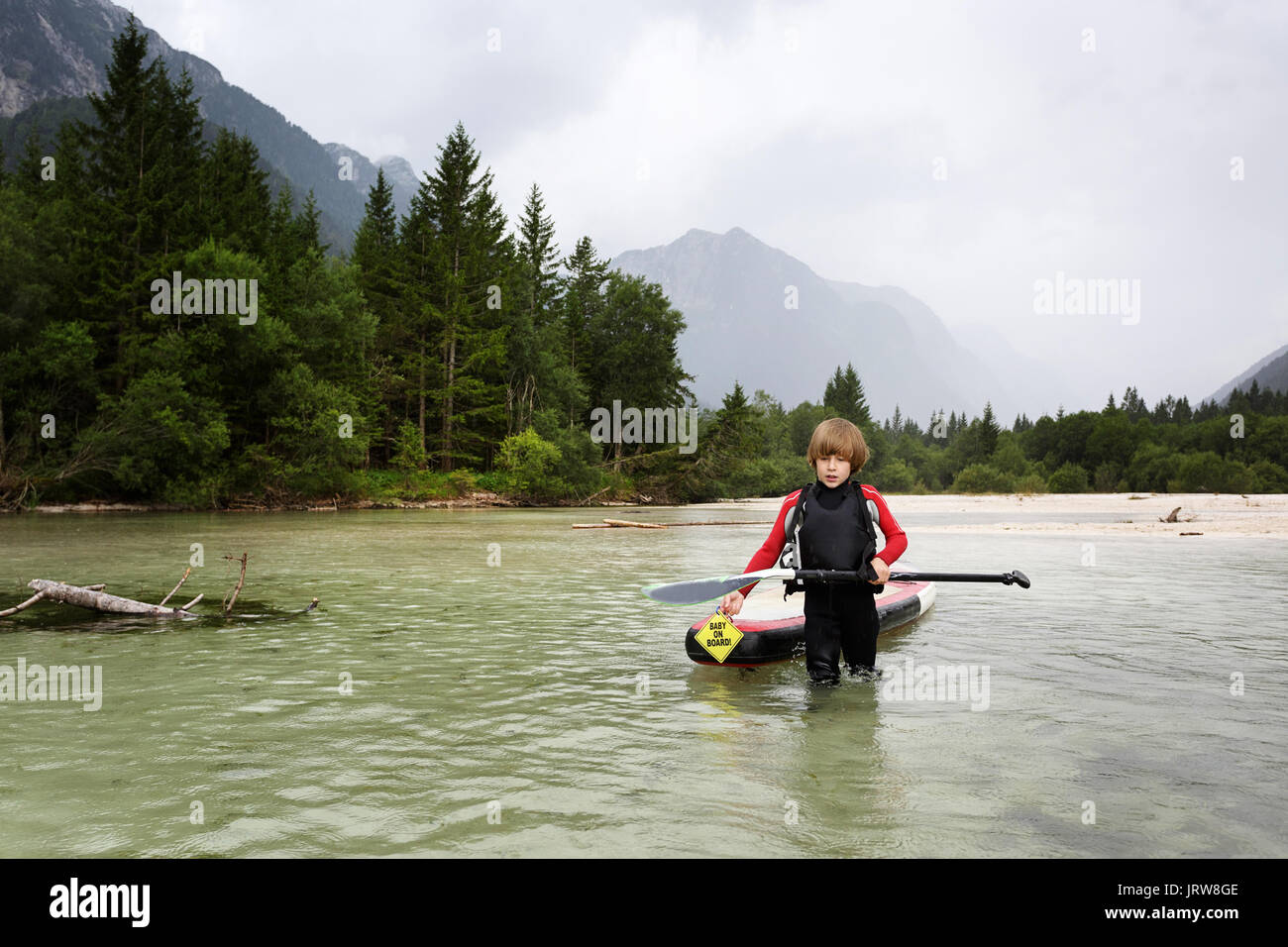 Young boy carrying a paddle and pulling a SUP in the clear water of ...