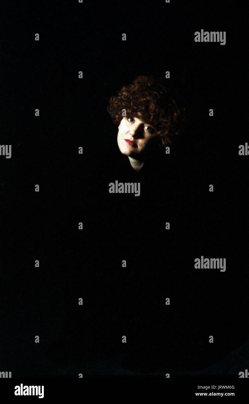 Dramatic dark studio portrait of a young woman’s pale face with red ...