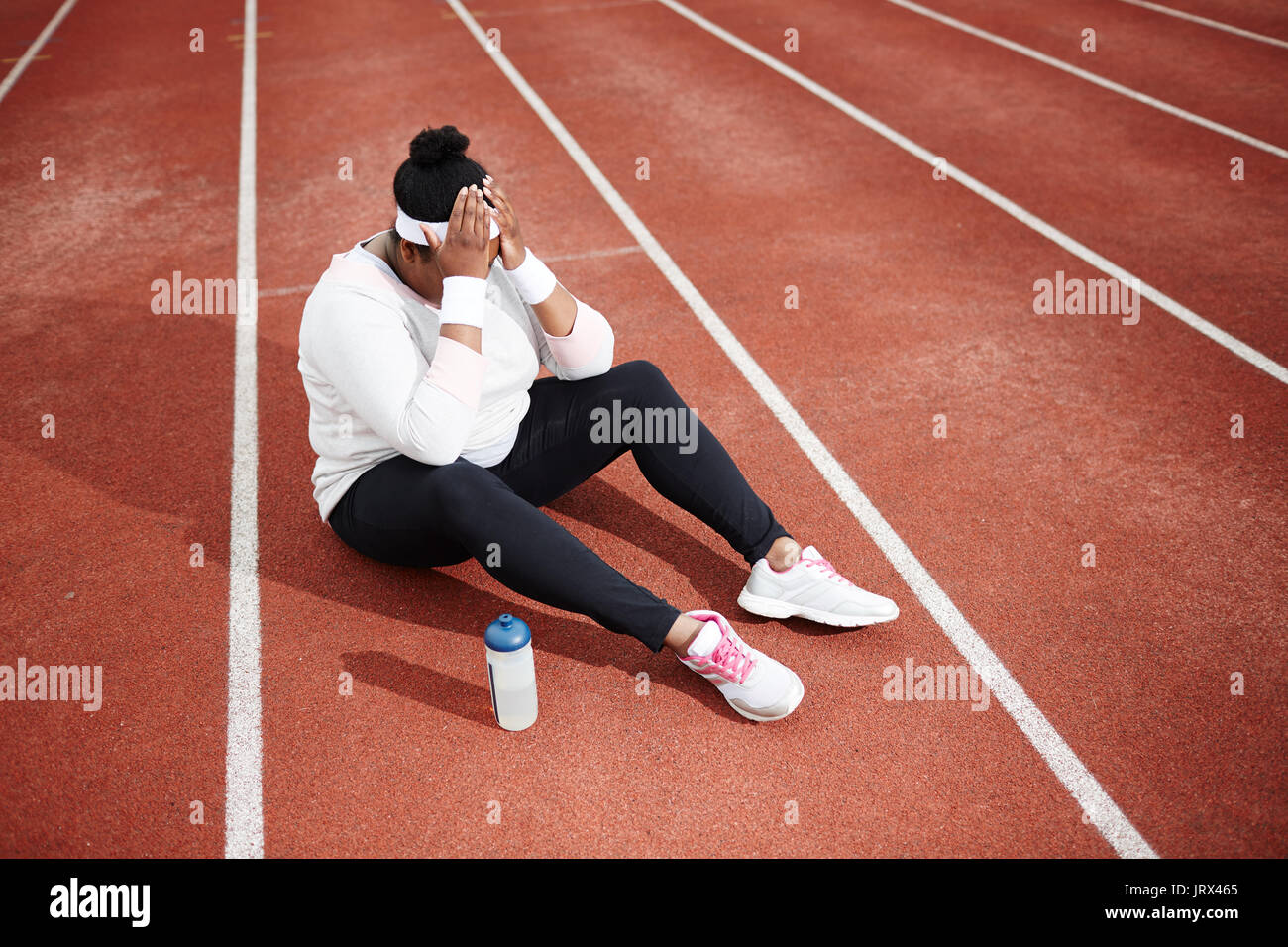 Frustrated overweight woman in sportswear sitting on running track ...