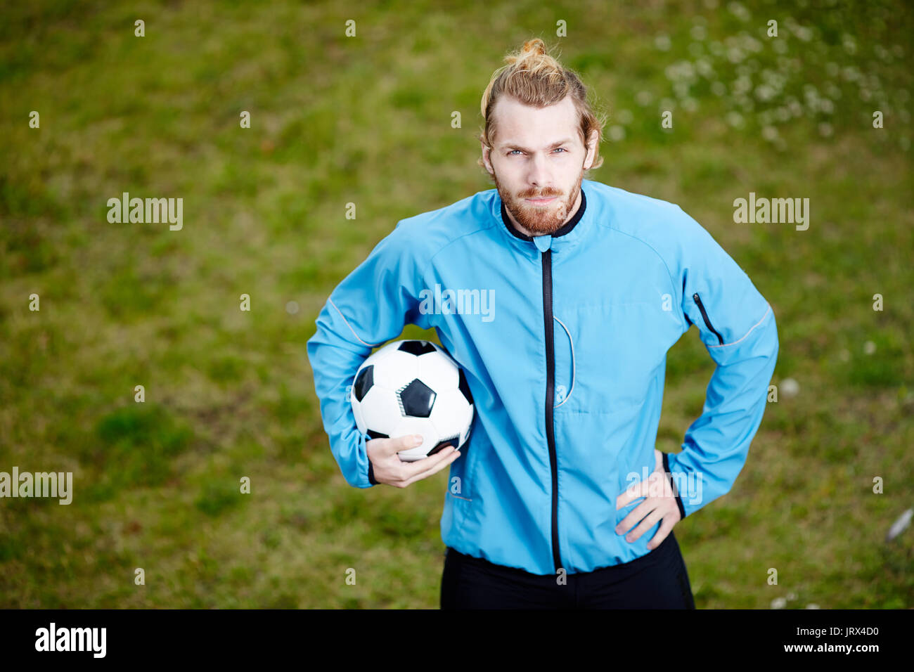 Portrait of young confident coach posing with ball at soccer field ...