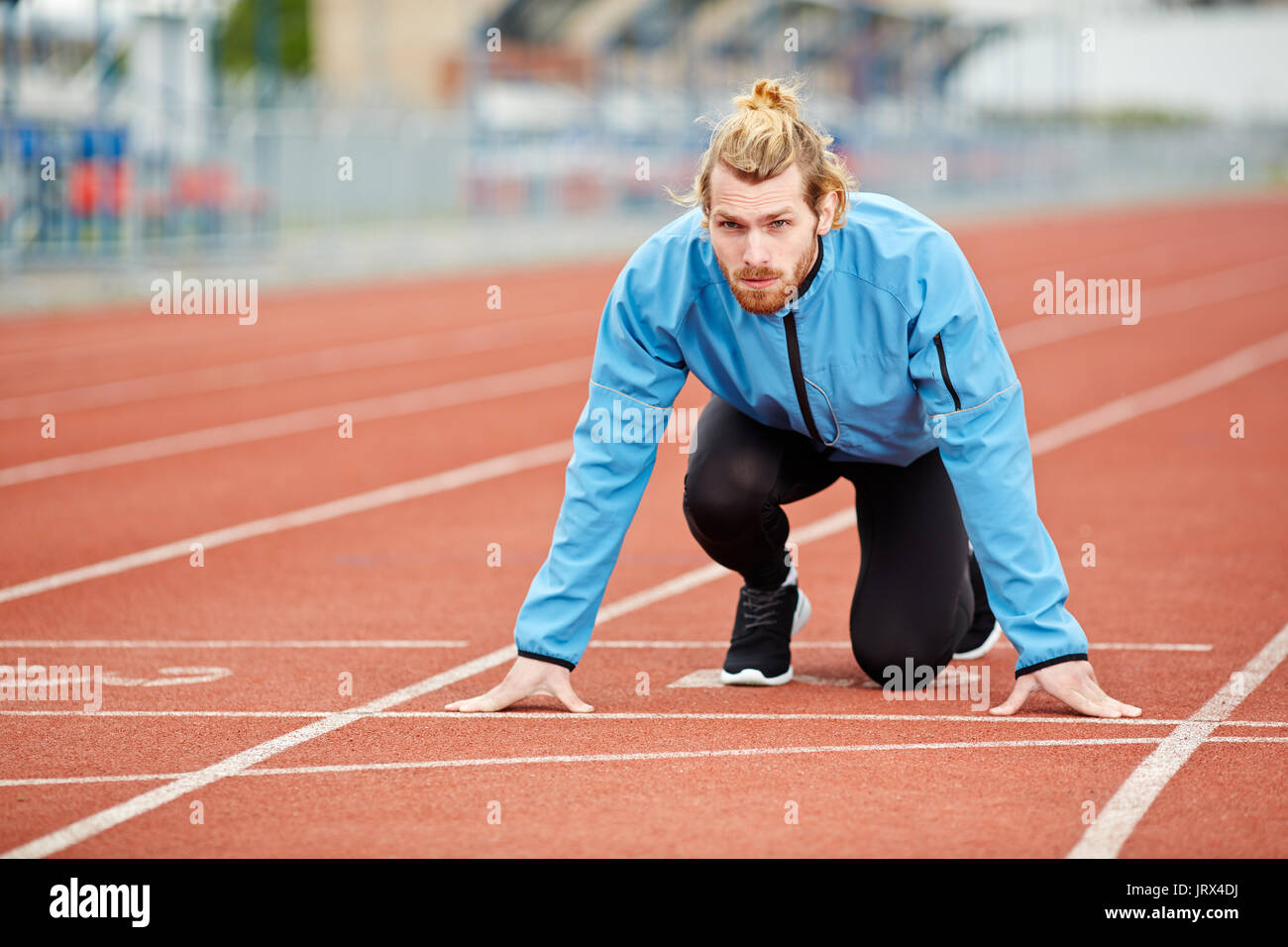 Determined young athlete on starting line at track and field stadium ...