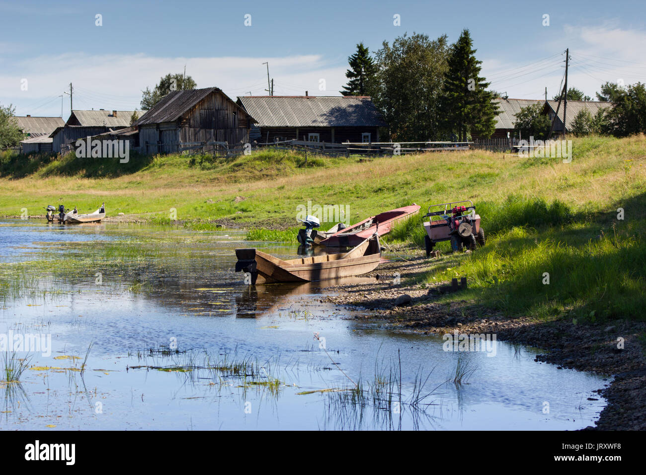 Sunny rural landscape with river, wooden handmade boats and houses ...