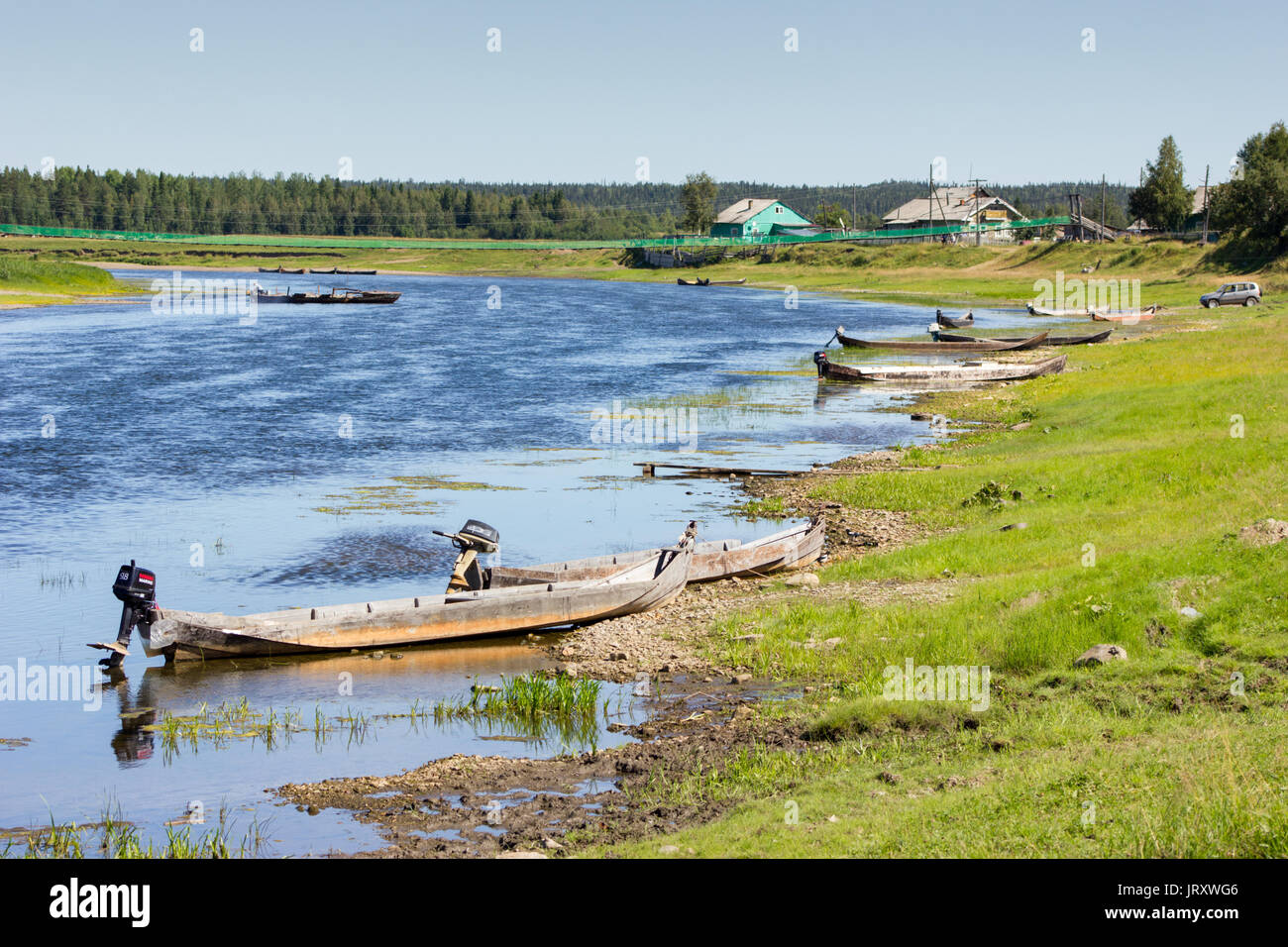 Sunny rural landscape with river, wooden handmade boats and houses ...