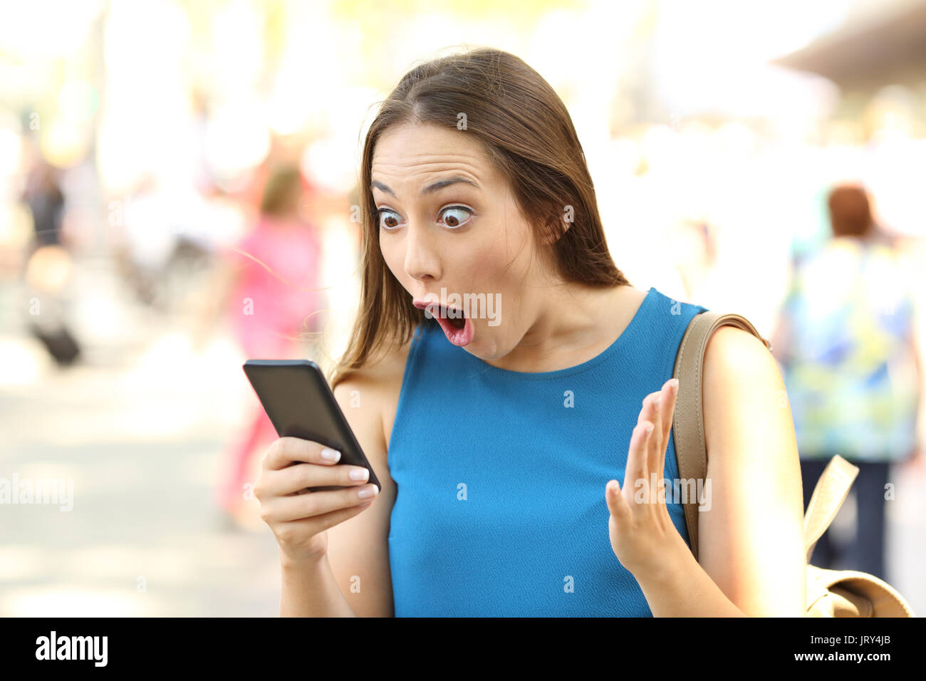 Amazed woman receiving shocking news on a smart phone on the street ...