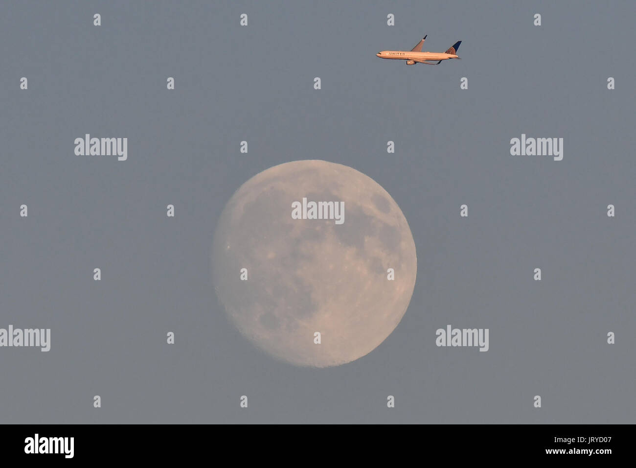 A United commercial passenger plane fly's past a full moon on route to ...