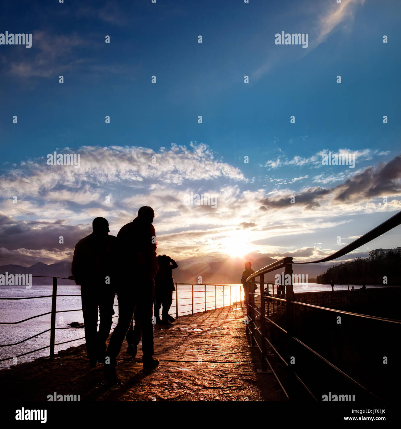 silhouetted people walking on street over sunset sky with sunbeam Stock ...