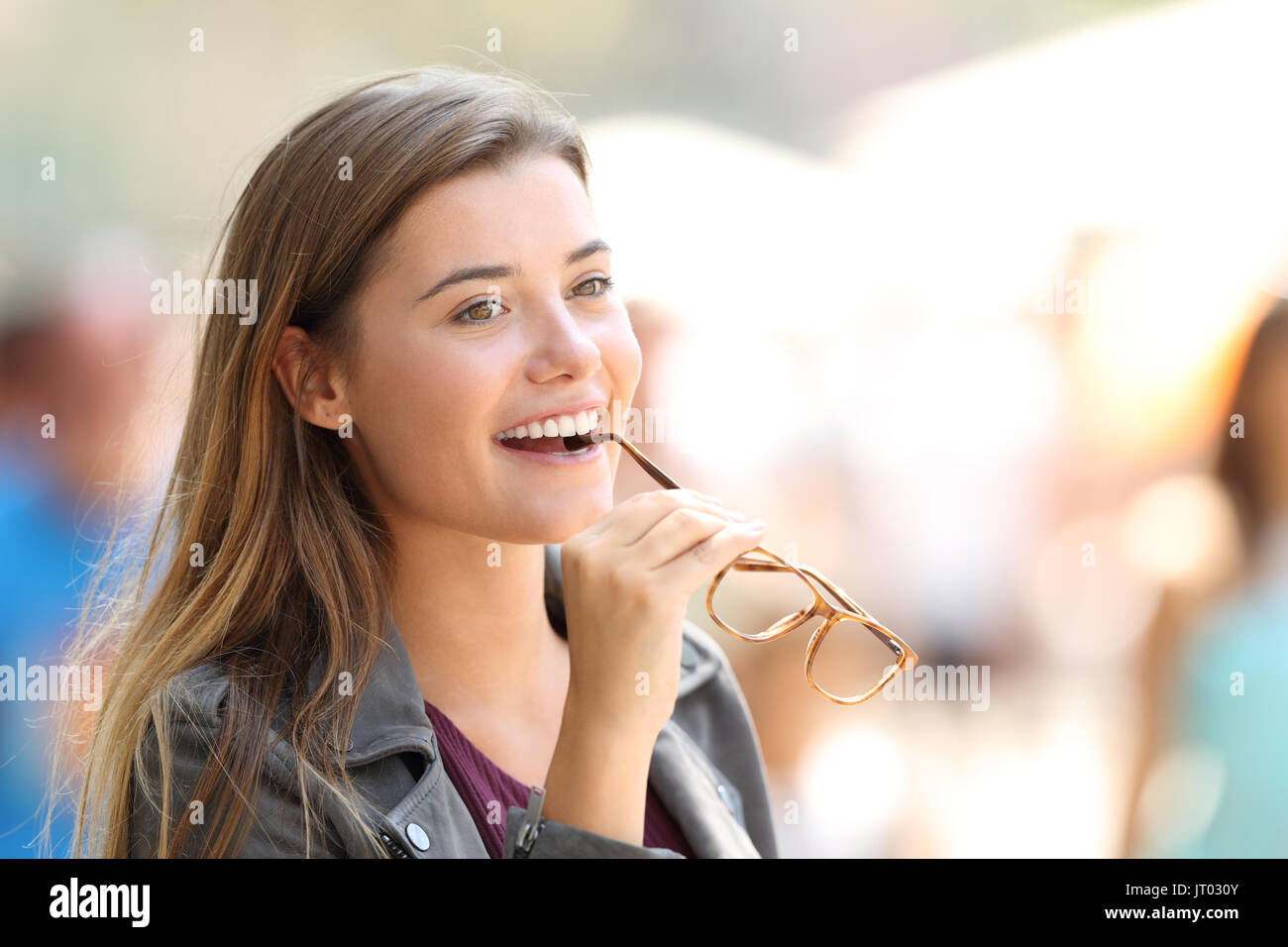 Portrait of a happy beautiful girl biting eyeglasses on the street ...